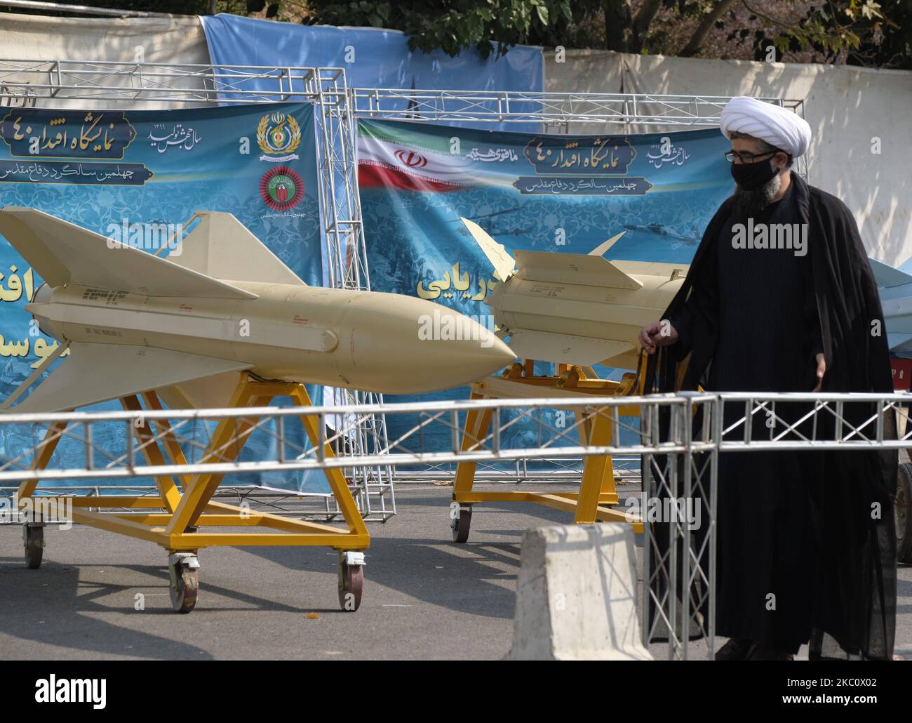 An Iranian cleric wearing a protective face mask walks past an anti ...