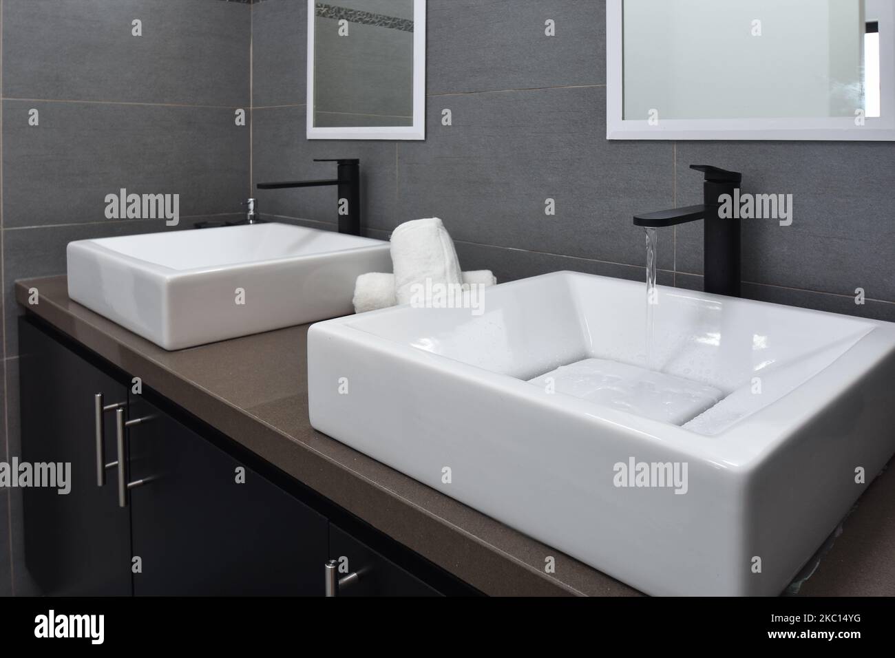 Square minimalistic sinks with flowing tap water and gray walls in the ...