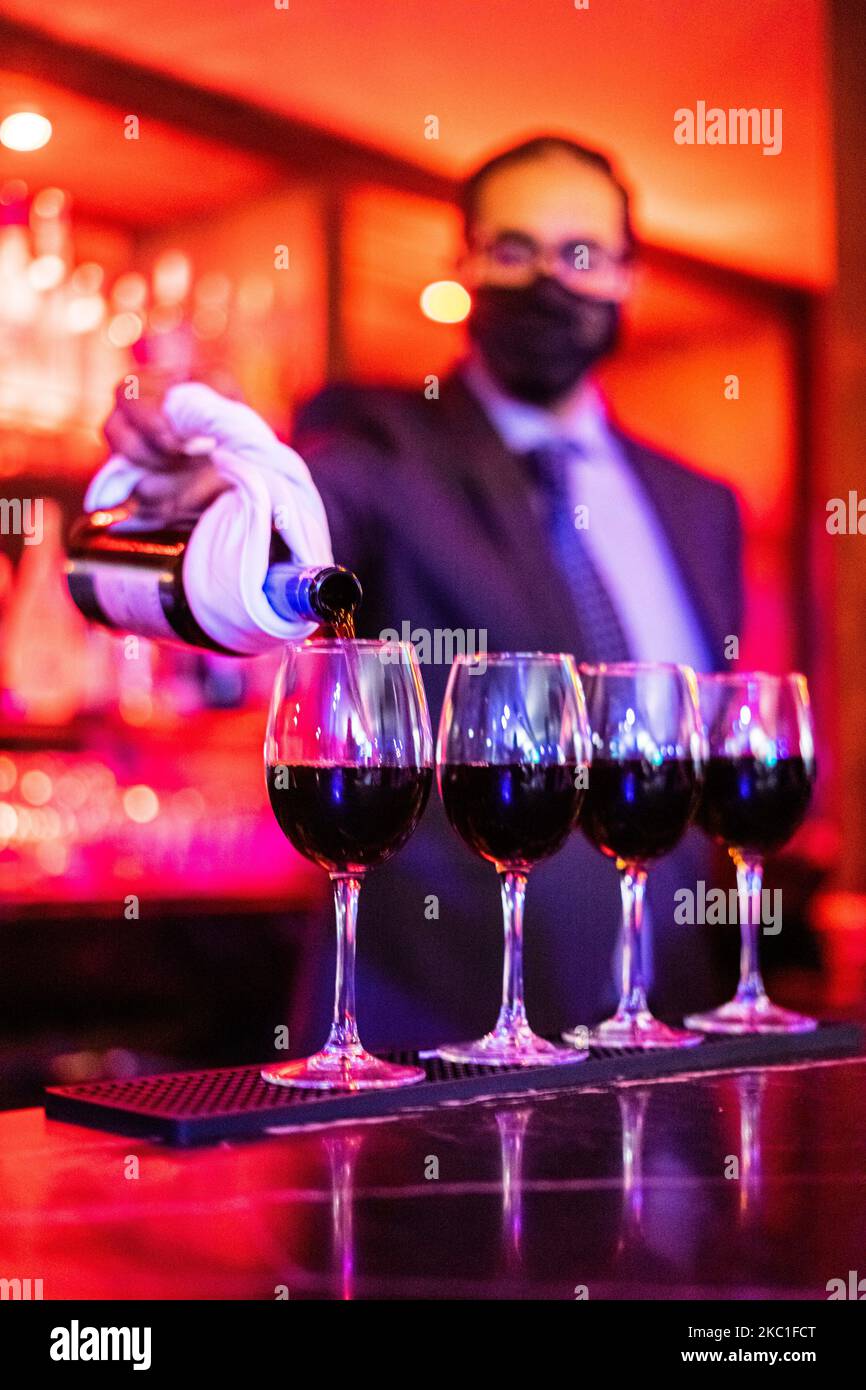 An adult man wearing face mask pouring red wine into the wineglasses ...