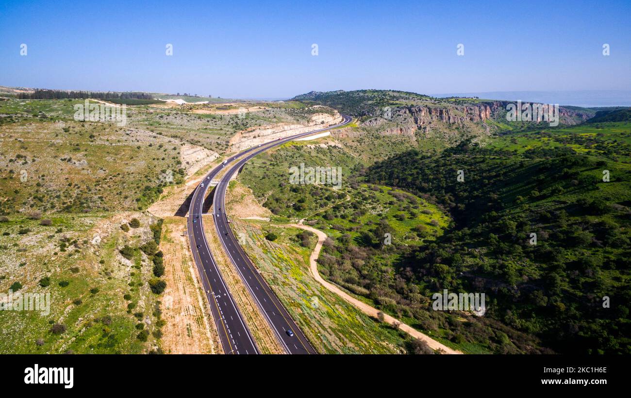 Aerial view shot flying over green hills fields, presents highway road ...