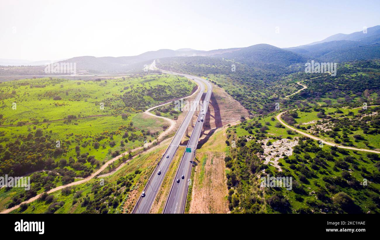 Aerial view shot flying over green hills fields, presents highway road ...