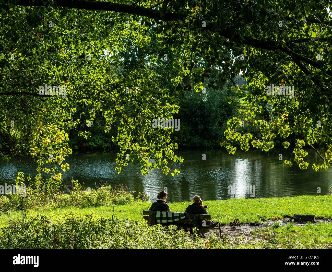 A couple of women are enjoying the sun, sitting on a bench close to a ...