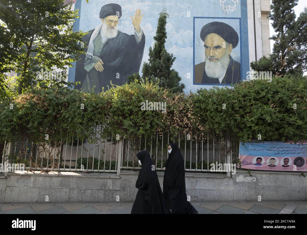Two Iranian veiled women wearing protective face masks walk under ...