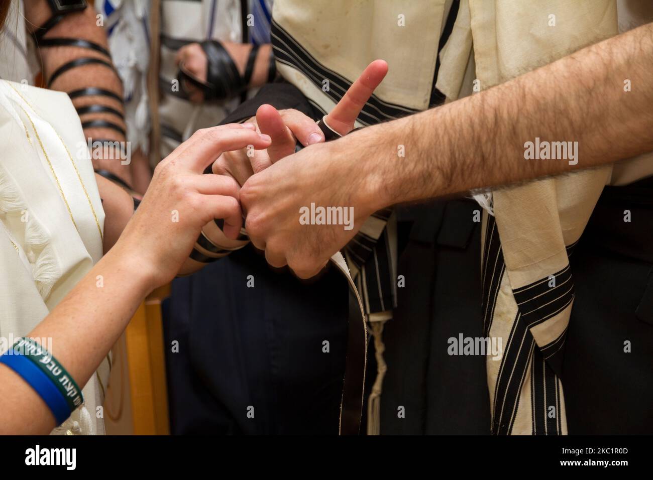 An orthodox man, wearing prayer shawl, put a Jewish Tefillin on A young ...