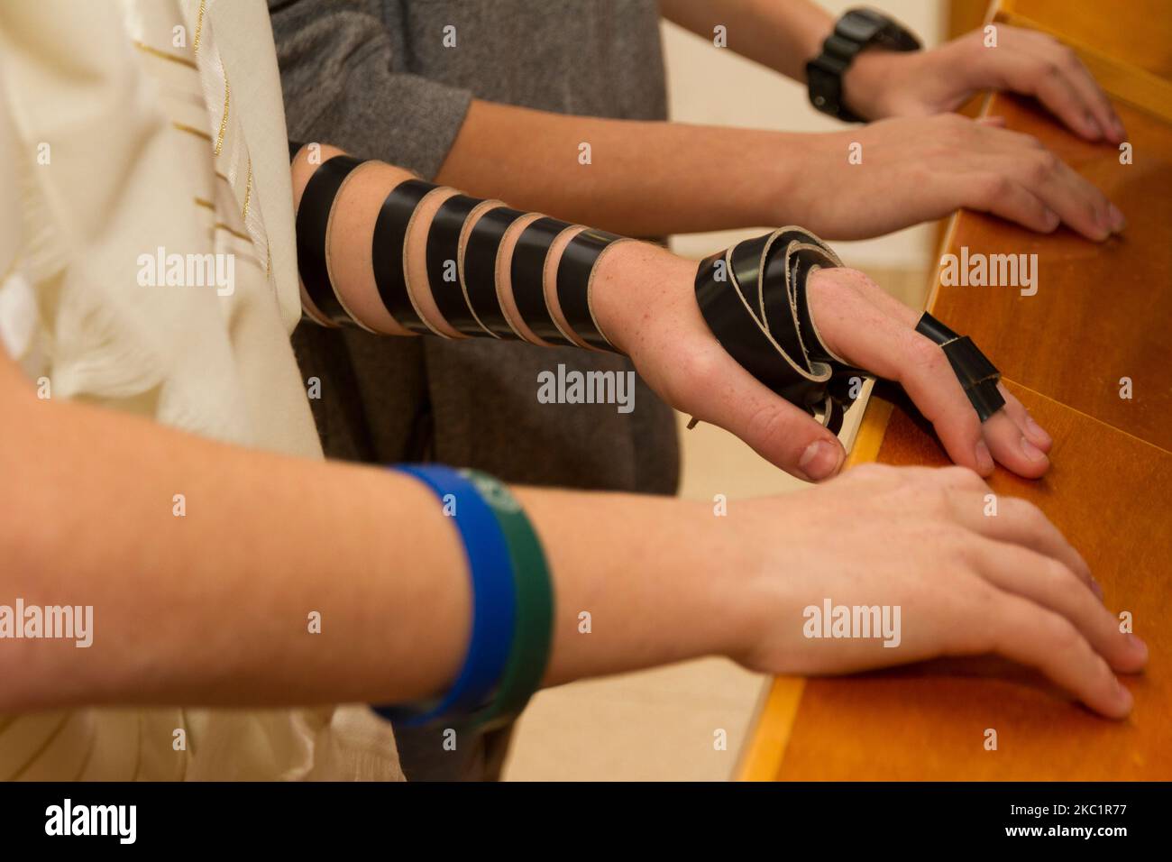 A young man using a Jewish Tefillin on his arm and wearing prayer shawl ...