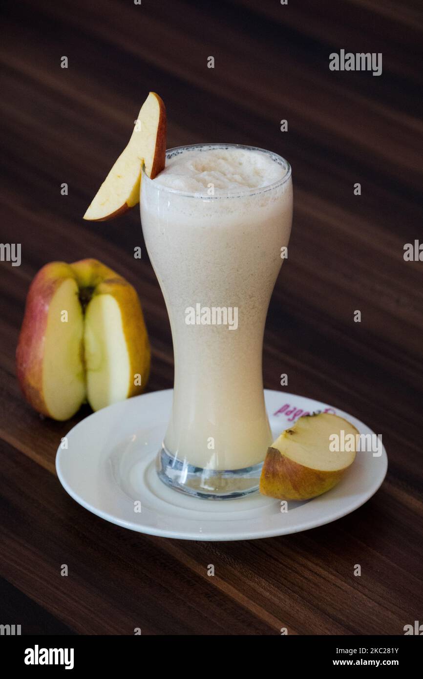 A vertical shot of apple smoothie in an elongated glass cup on a wooden ...