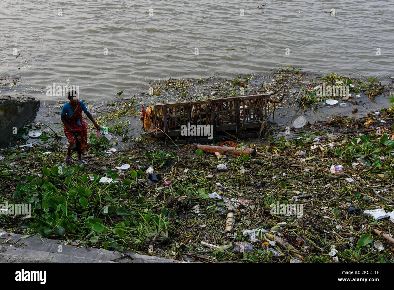 A lady makes her way through a garbage pile that rests at a river side ...