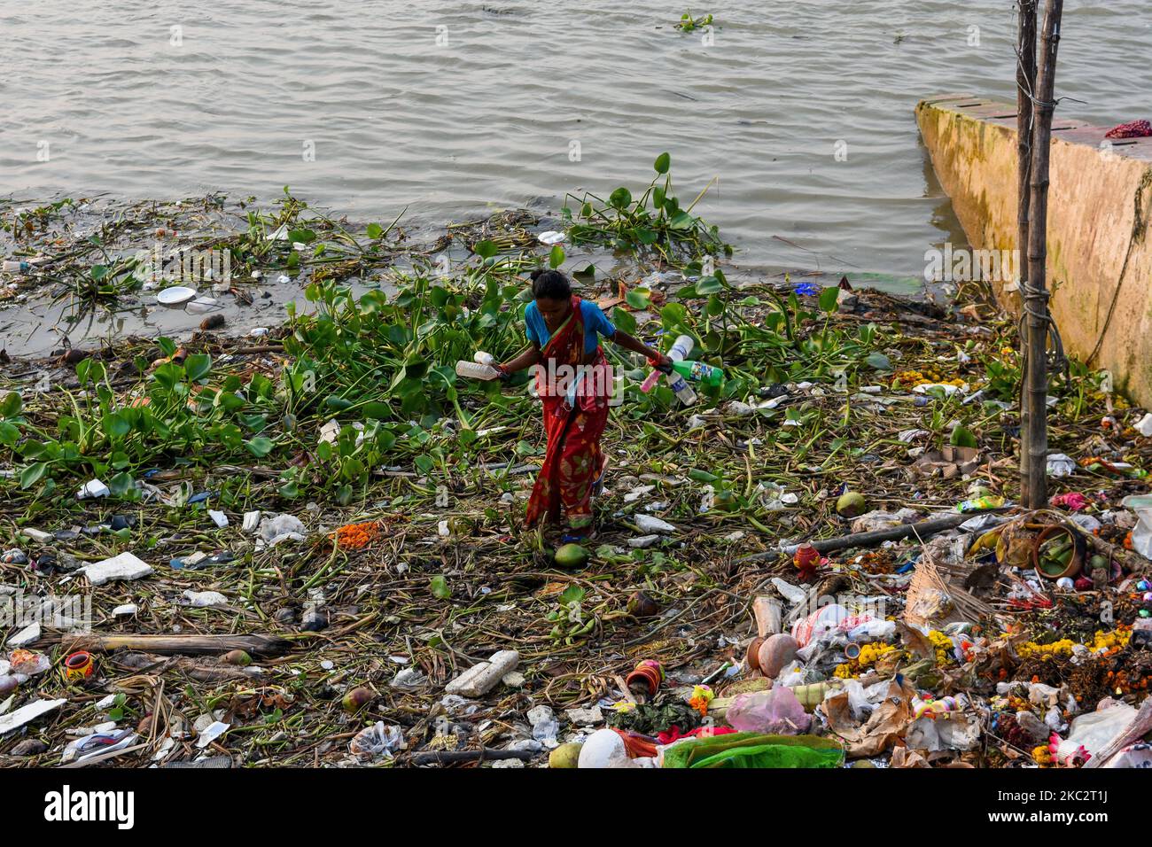 A lady makes her way through a garbage pile that rests at a river side ...