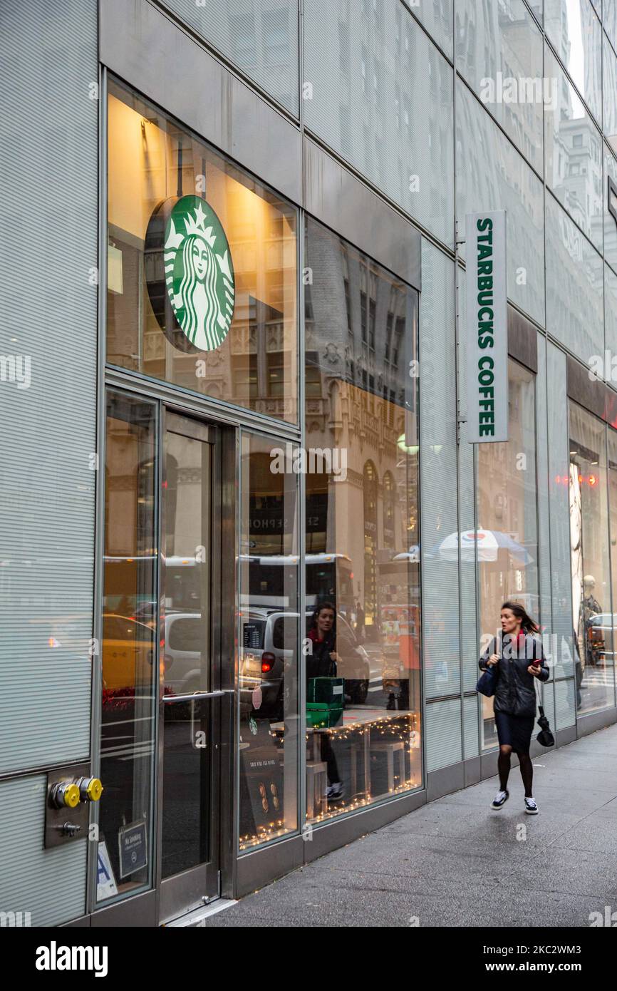A woman walking next to a store front of a Starbucks Coffee shop ...