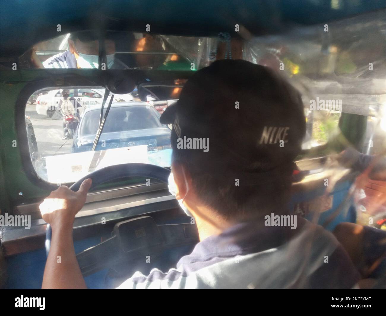 A plastic divider separates a Filipino jeepney driver wearing a ...