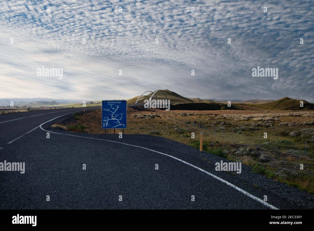A blue sign by the empty country road with the bridge and hills in the ...