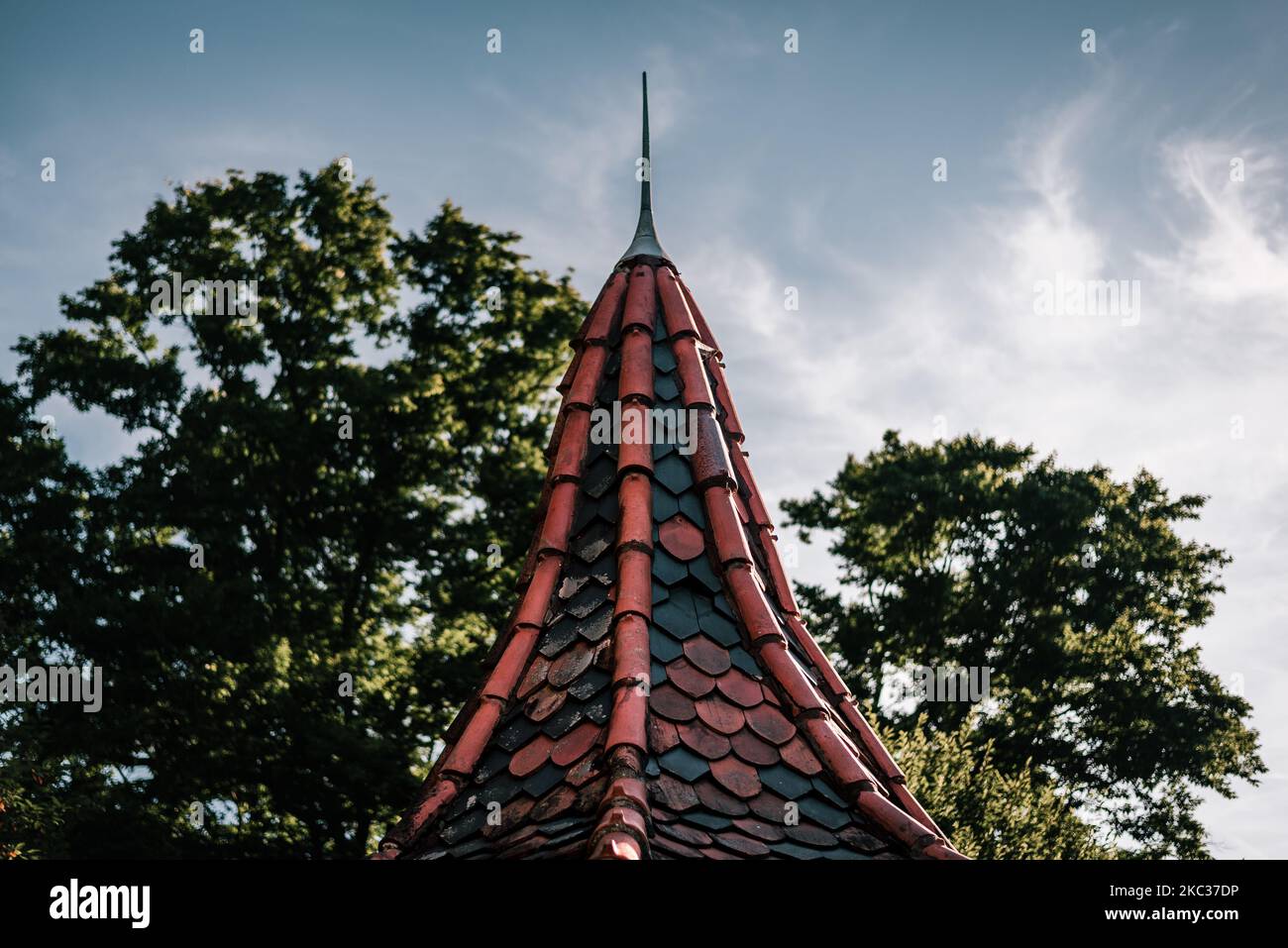 A pointed roof with orange tiles of a building with trees in the ...