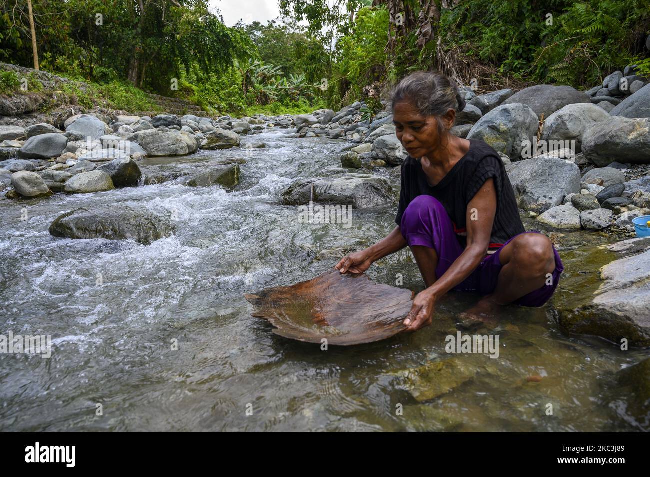 A mother panning gold with traditional tools in Powelua Village ...