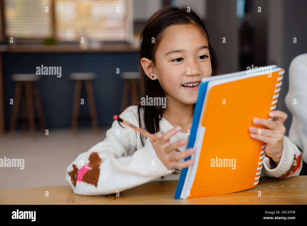 Asian girl smiling and doing homework while sitting at table at home Stock Photo - Alamy