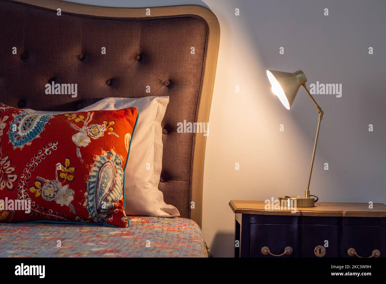 A vintage bed corner with a brown headboard, antique style pillows, and ...