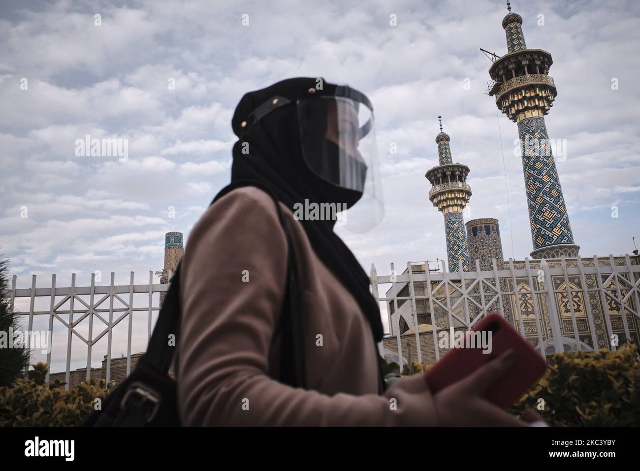 An Iranian woman wearing a protective face mask and a face shield walks ...
