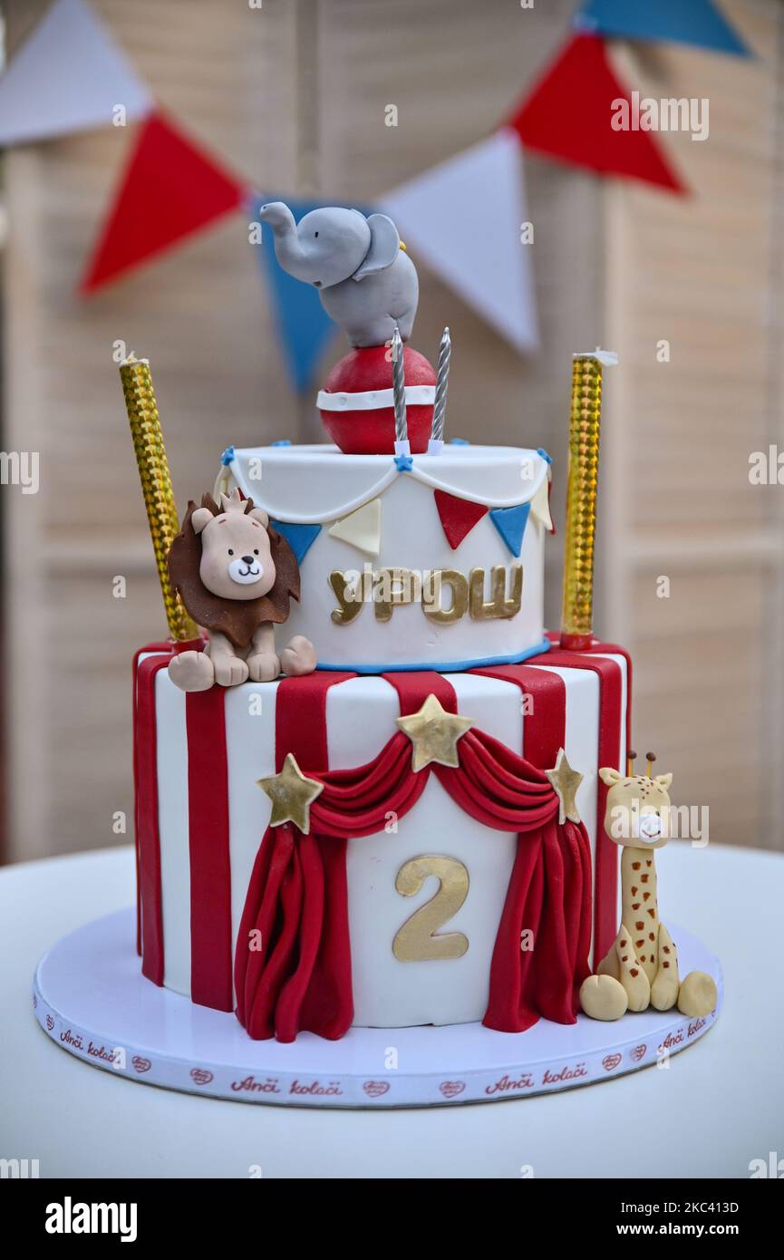 A two-tier birthday cake in a circus design with fireworks and candles ...