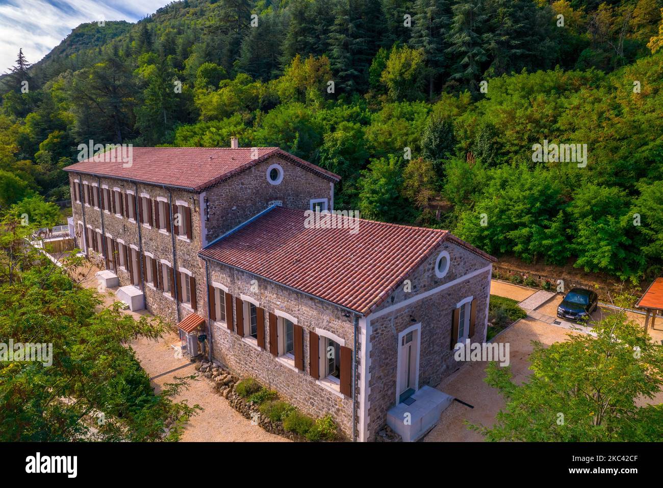 An aerial view of a long red stone villa on a hill full of trees and ...