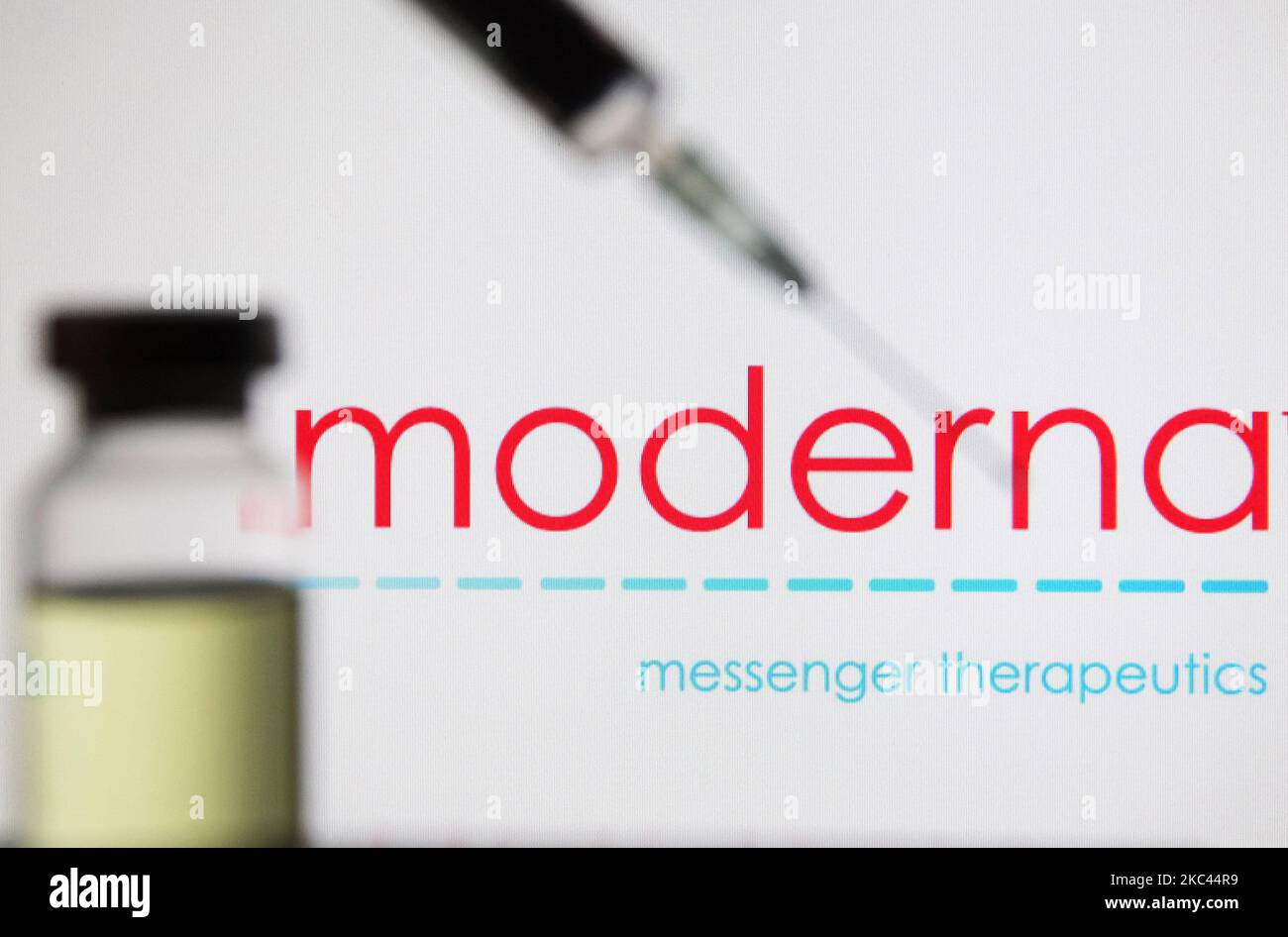 A medical syringe and a vial in front of the Moderna logo are seen in ...