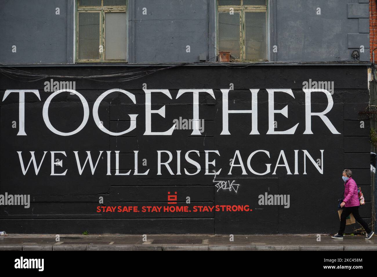A woman walks by a mural stating 'Together We Will rise Again' - seen ...