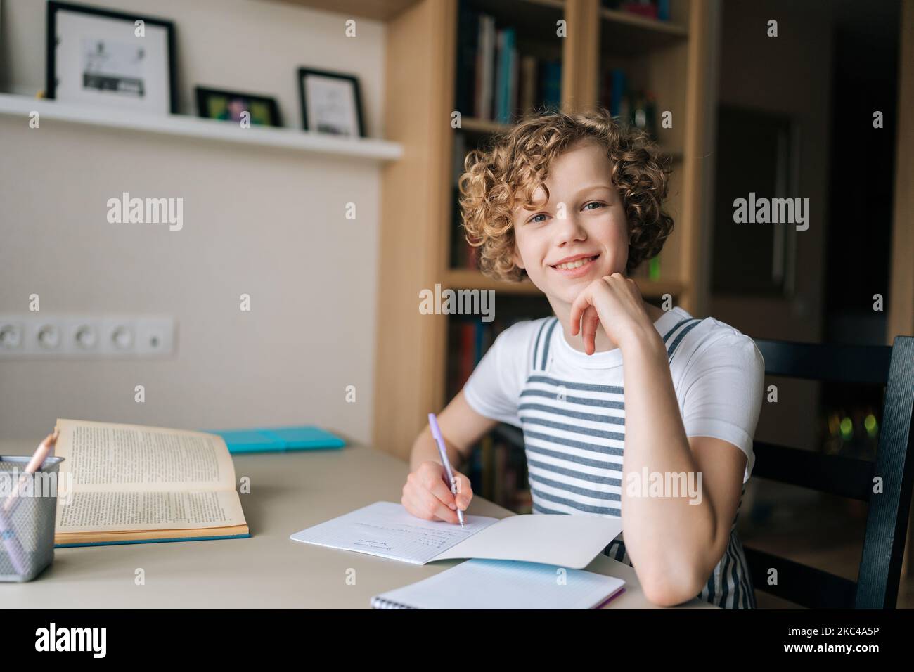 Medium shot portrait of smiling curly little schoolgirl studying at ...