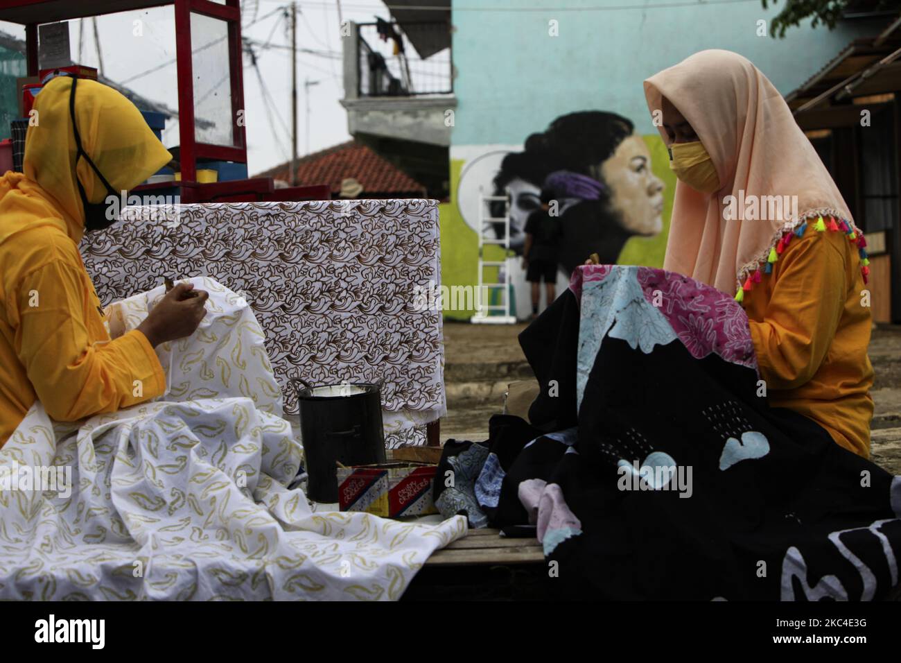 Batik craftsmen works on a batik with a graffiti background on a wall ...