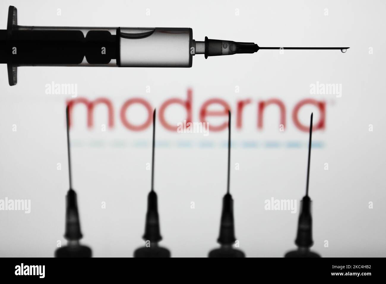 Medical syringes are seen with Moderna logo displayed on a screen in ...