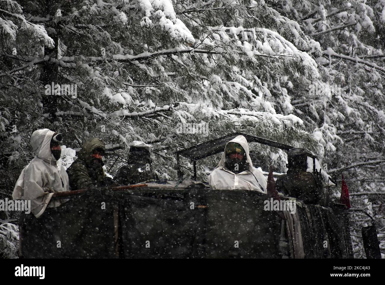 Indian army soldiers stand atop of a military vehicle during snowfall ...