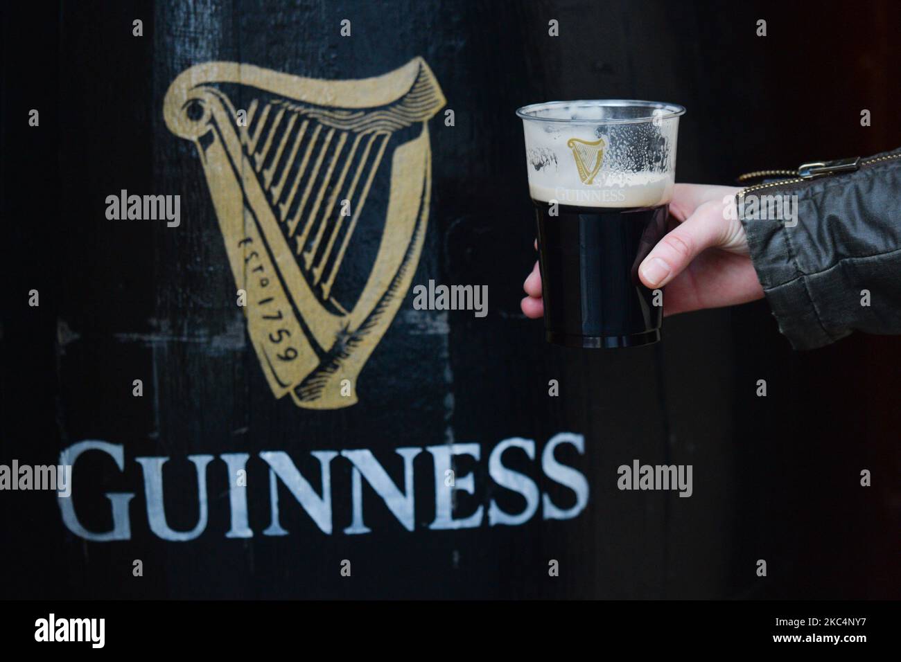 A person enjoys a pint of Guinness in a plastic cup outside a pub in ...