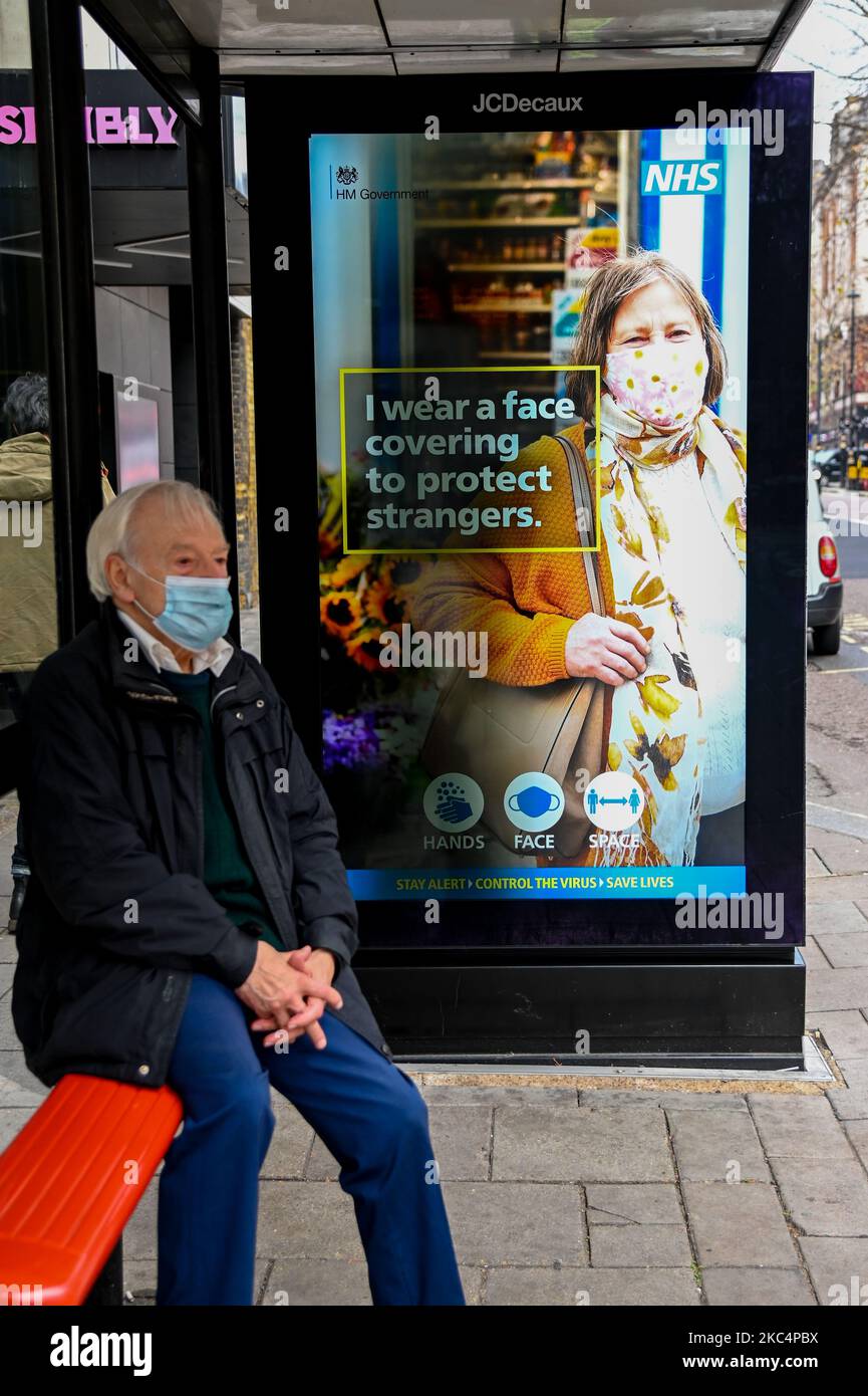 A man wearing a face mask as a precaution at a bus stop with an ...
