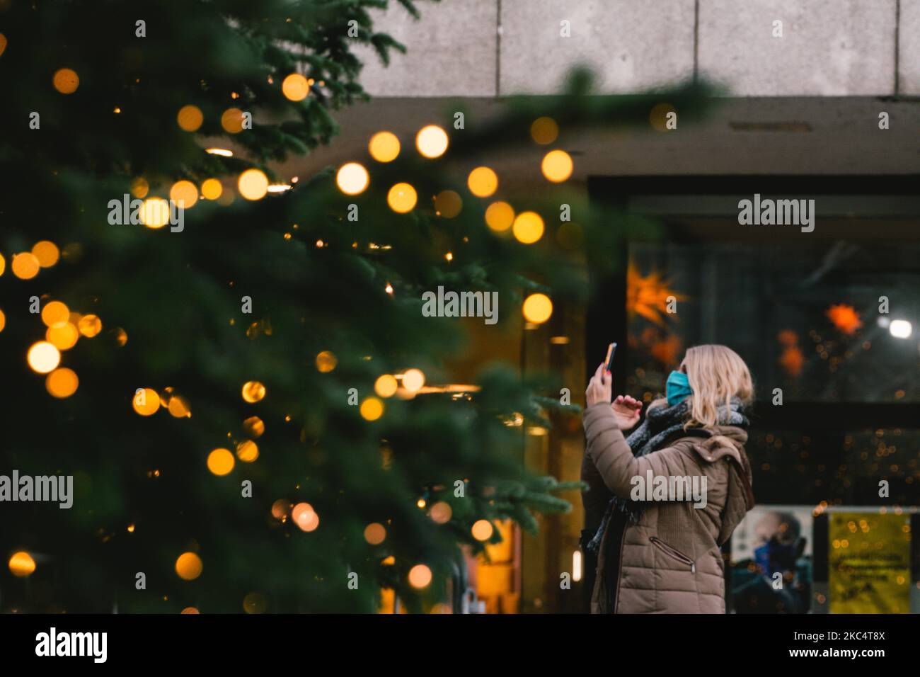 a woman with face mask take cell phone photo of a Christmas tree in ...