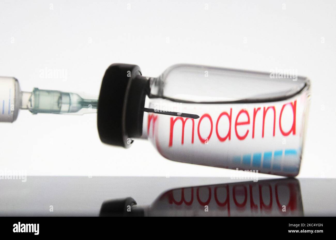 A medical syringe and a vial in front of the Moderna logo are seen in ...