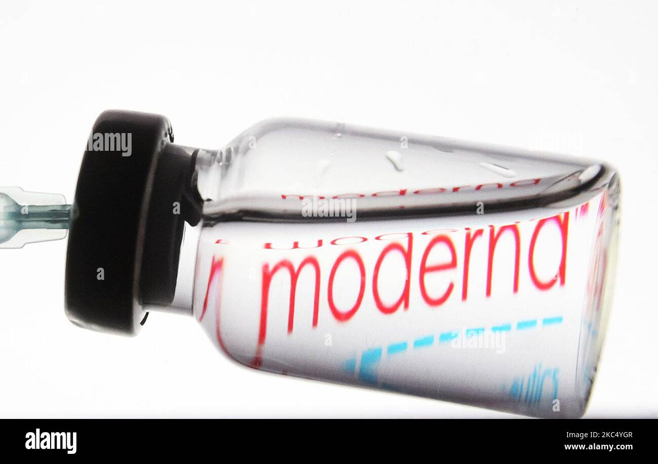 A medical syringe and a vial in front of the Moderna logo are seen in ...