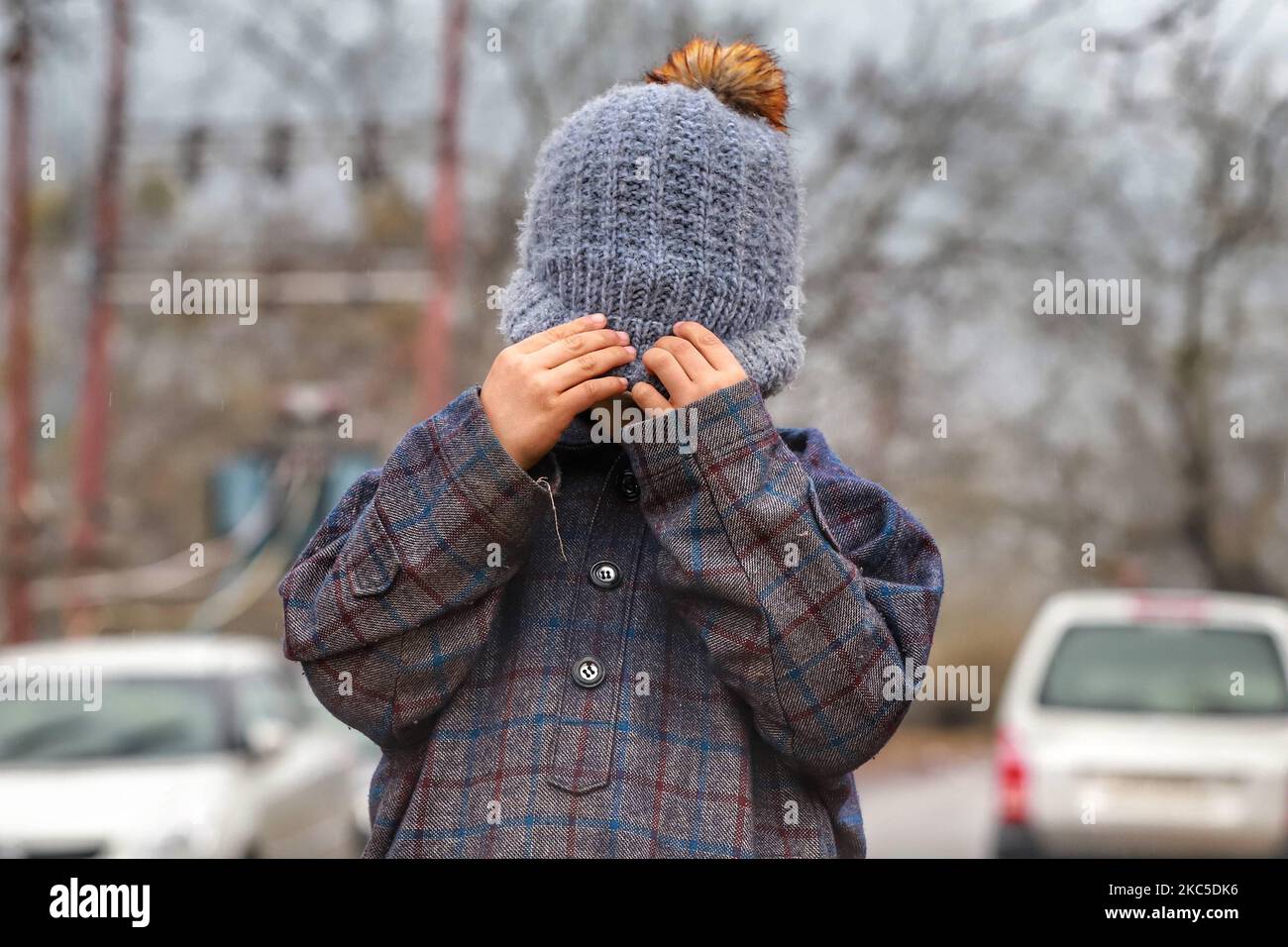 A Kashmiri boy wearing a Feran (Woolen Outfit) hides his face with a ...