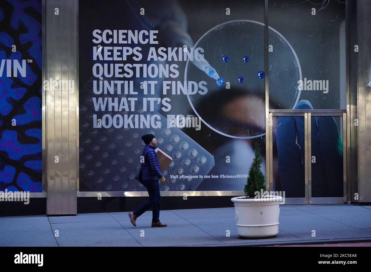 A view of people wearing masks walking past a Pfizer poster in front of ...