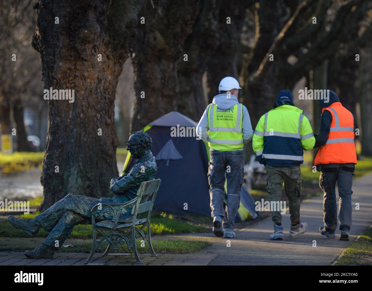 Three construction workers walk by a rough sleeper's tent next to the ...