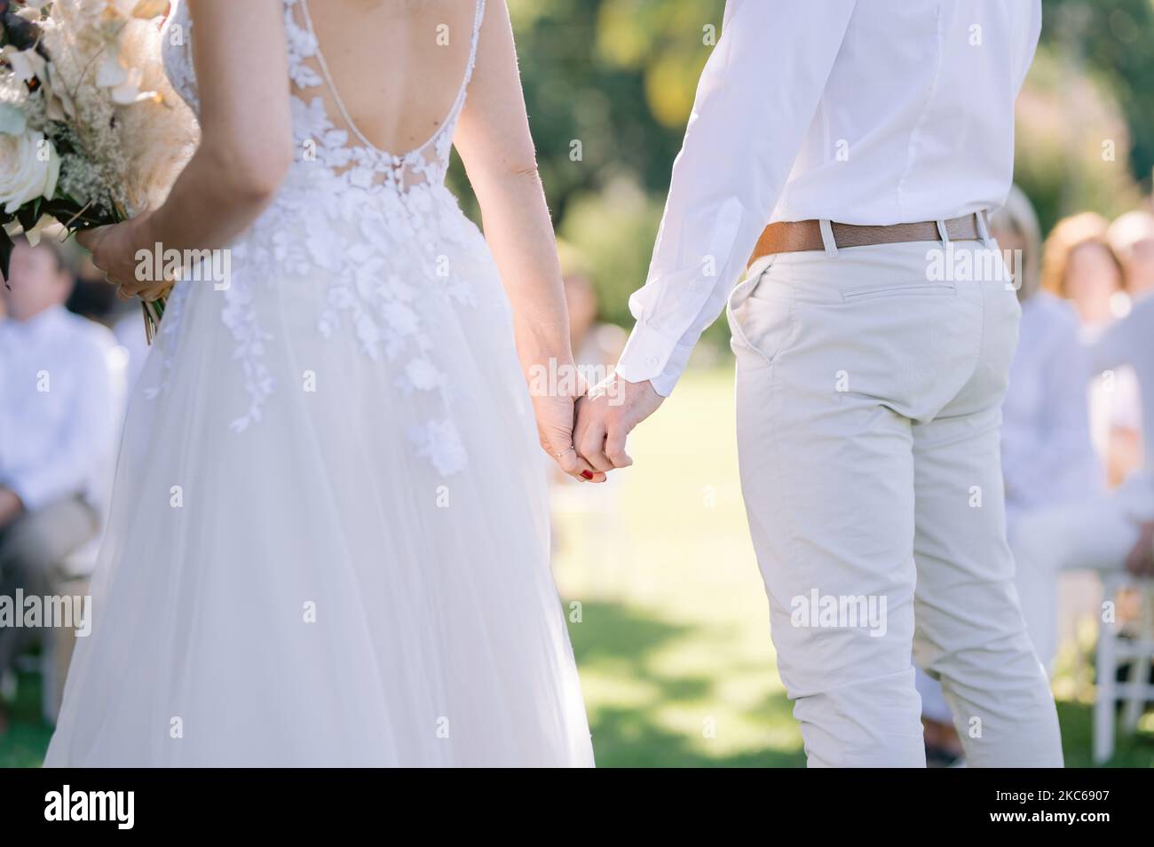 A bride and a groom both dressed in white holding hands at their ...