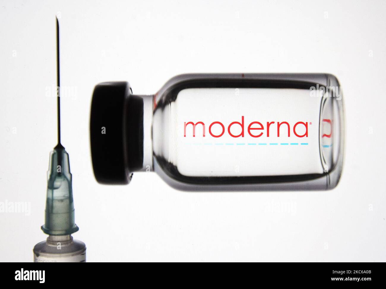 A medical syringe and a vial are seen in front of Moderna logo in this ...