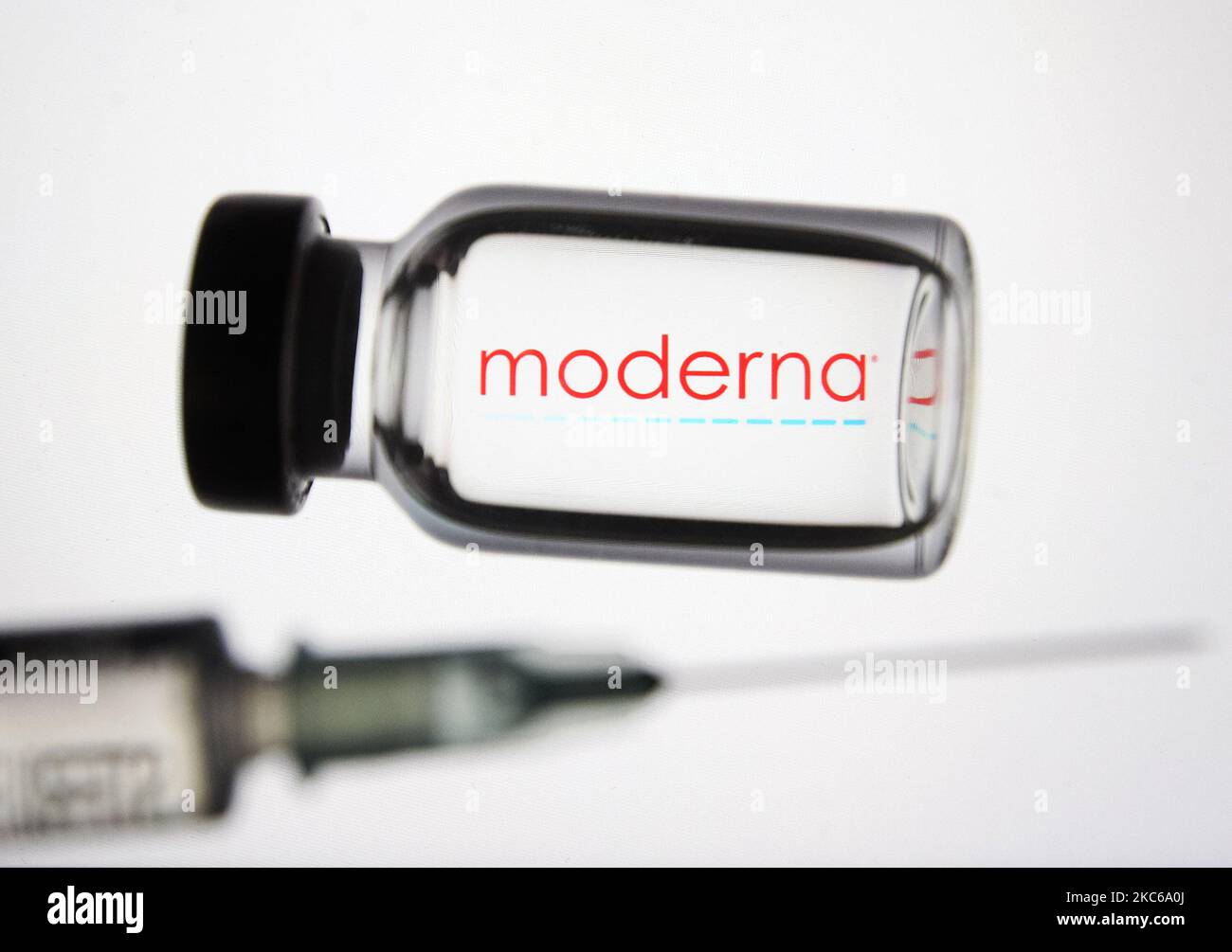 A medical syringe and a vial are seen in front of Moderna logo in this ...