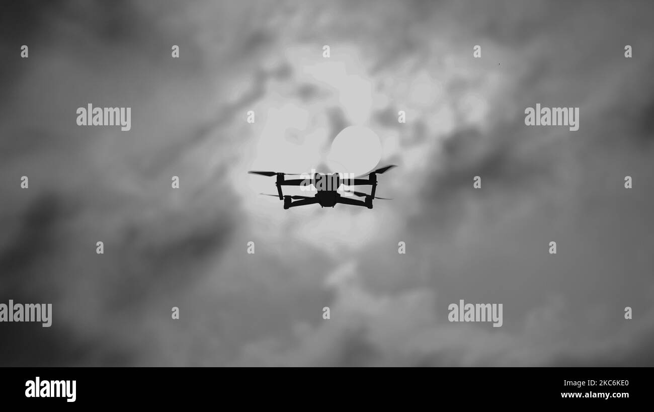 A grayscale shot of the silhouette of a drone flying towards the sun in ...
