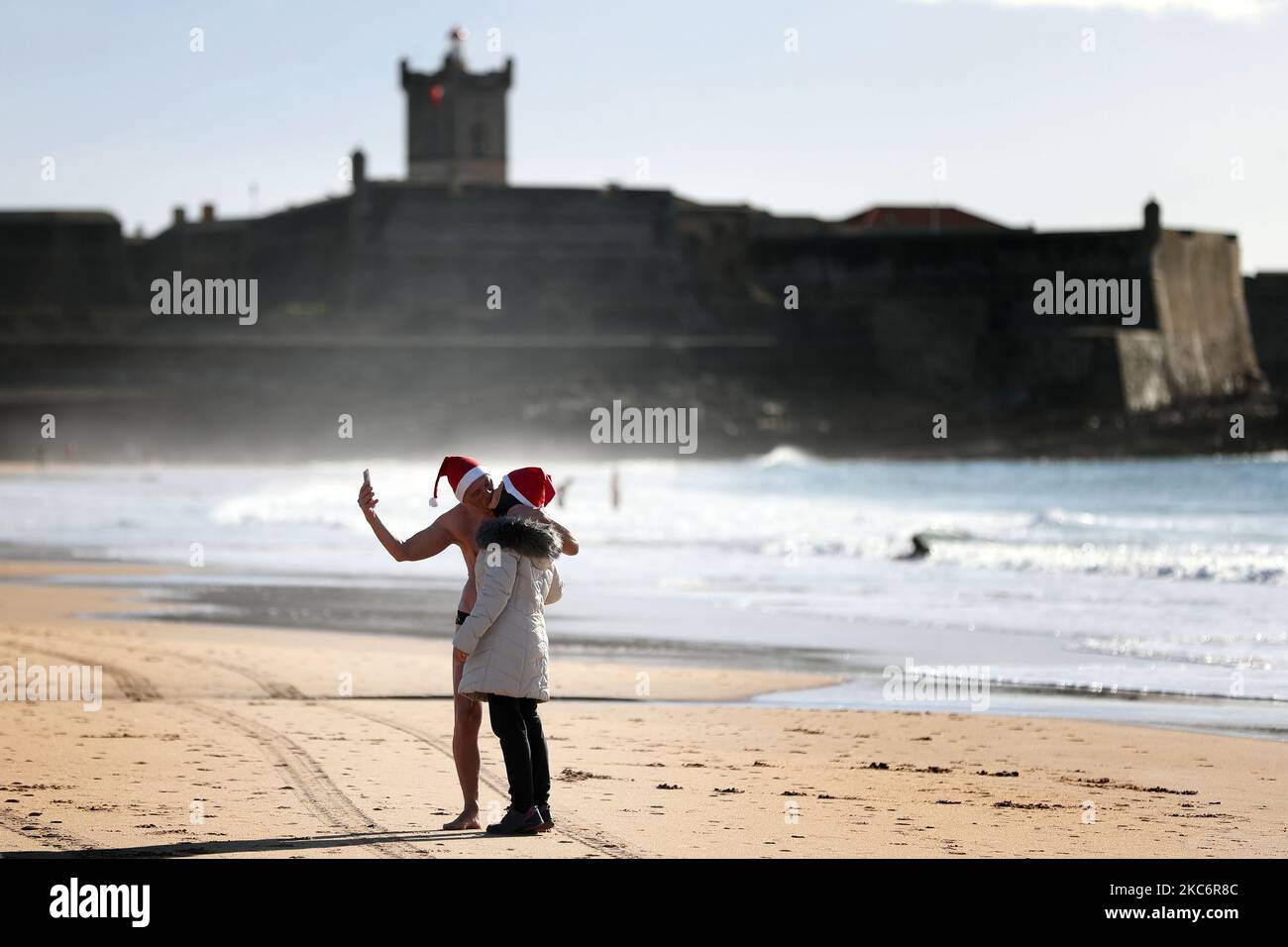 A couple wearing Santa Claus hats kisses during a traditional sea bath ...