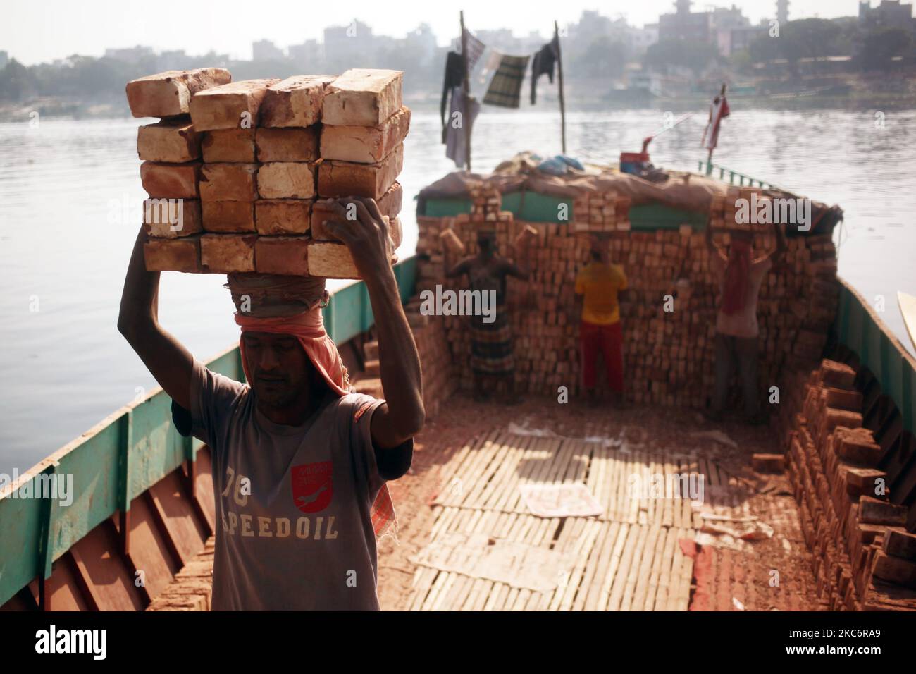 Laborers unload bricks from a cargo ship at Kamrangirchar area in Dhaka ...