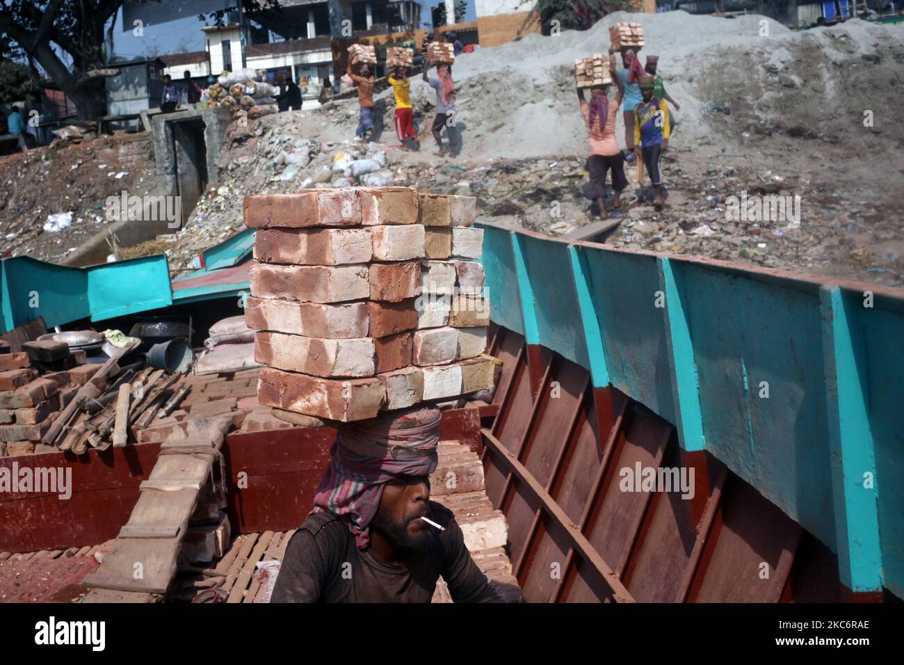 Laborers unload bricks from a cargo ship at Kamrangirchar area in Dhaka ...