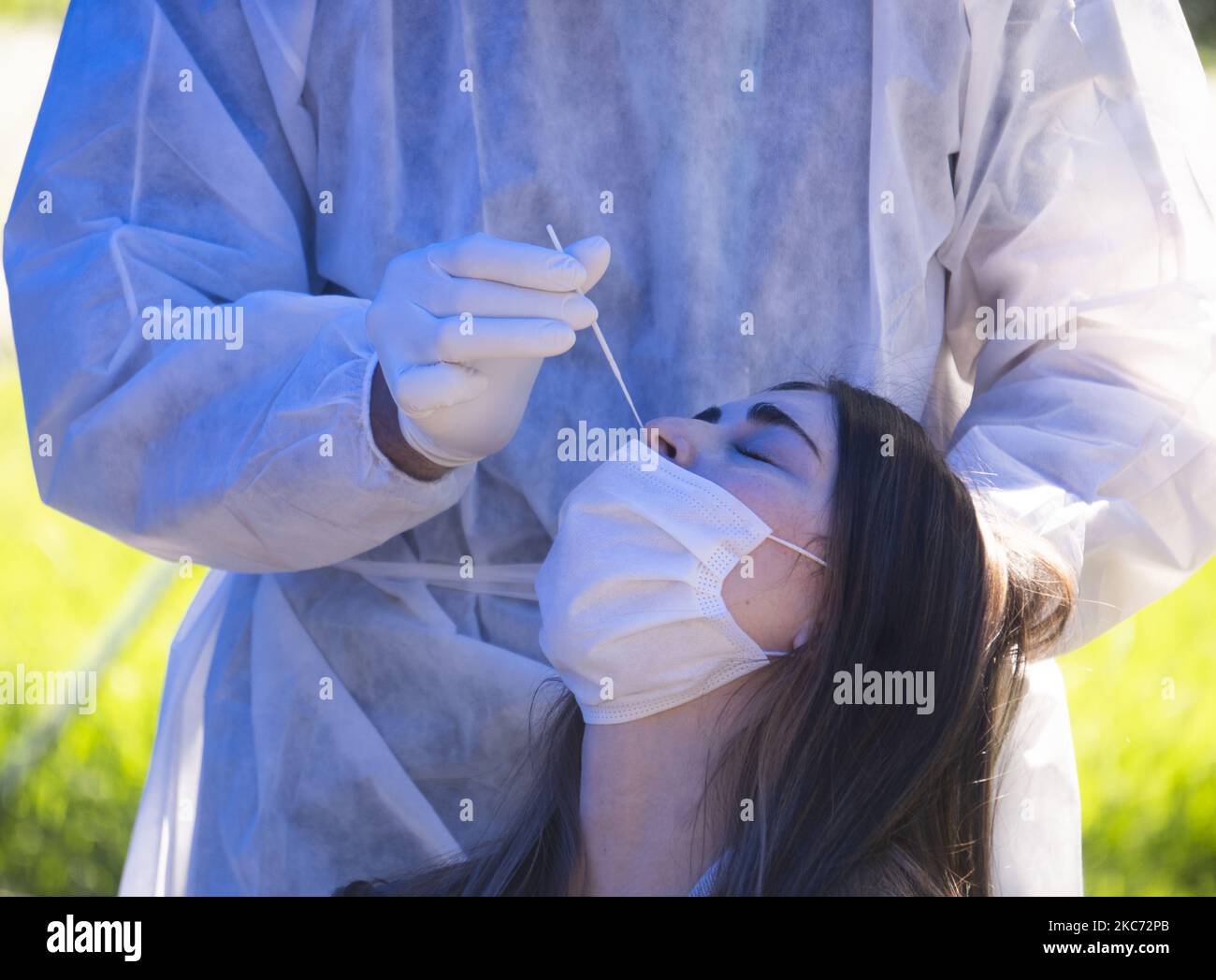 A nurse inserts a swab into a person's nose performing a PCR test for ...