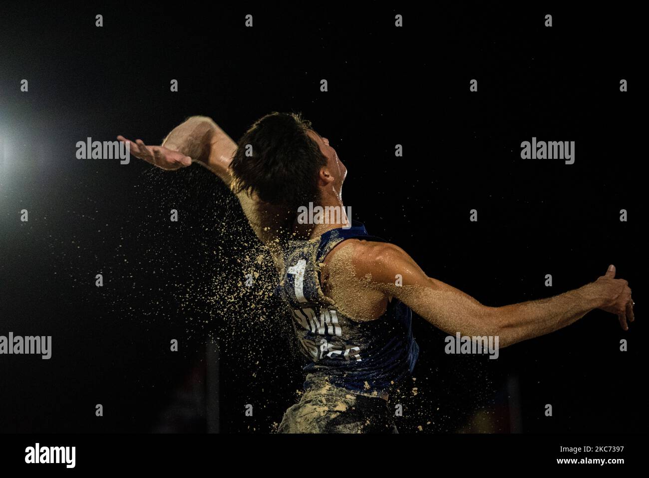 A volleyball player spiking a ball with sand flying off his back and ...