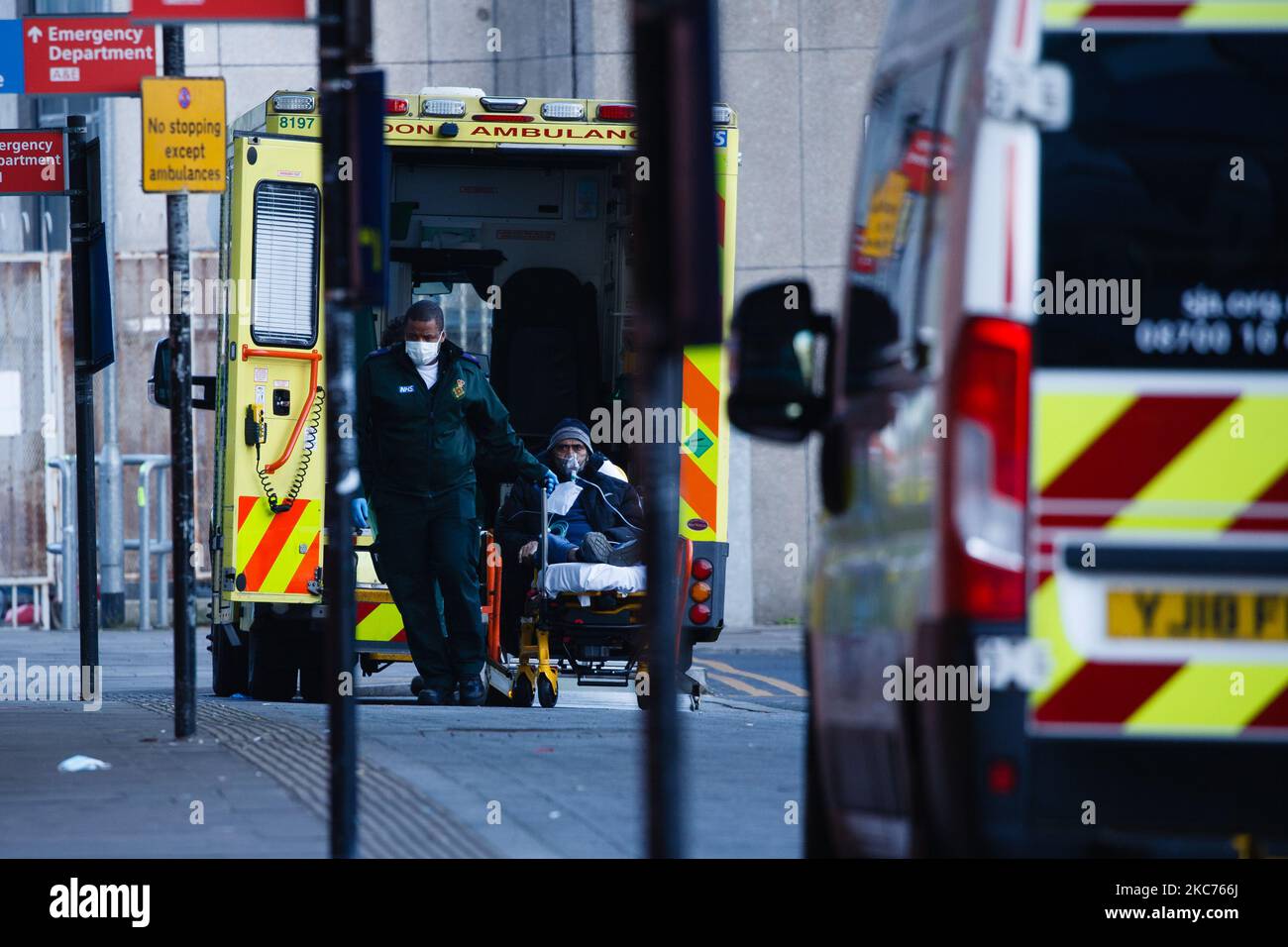 Paramedics wheel a patient wearing an oxygen mask from an ambulance ...
