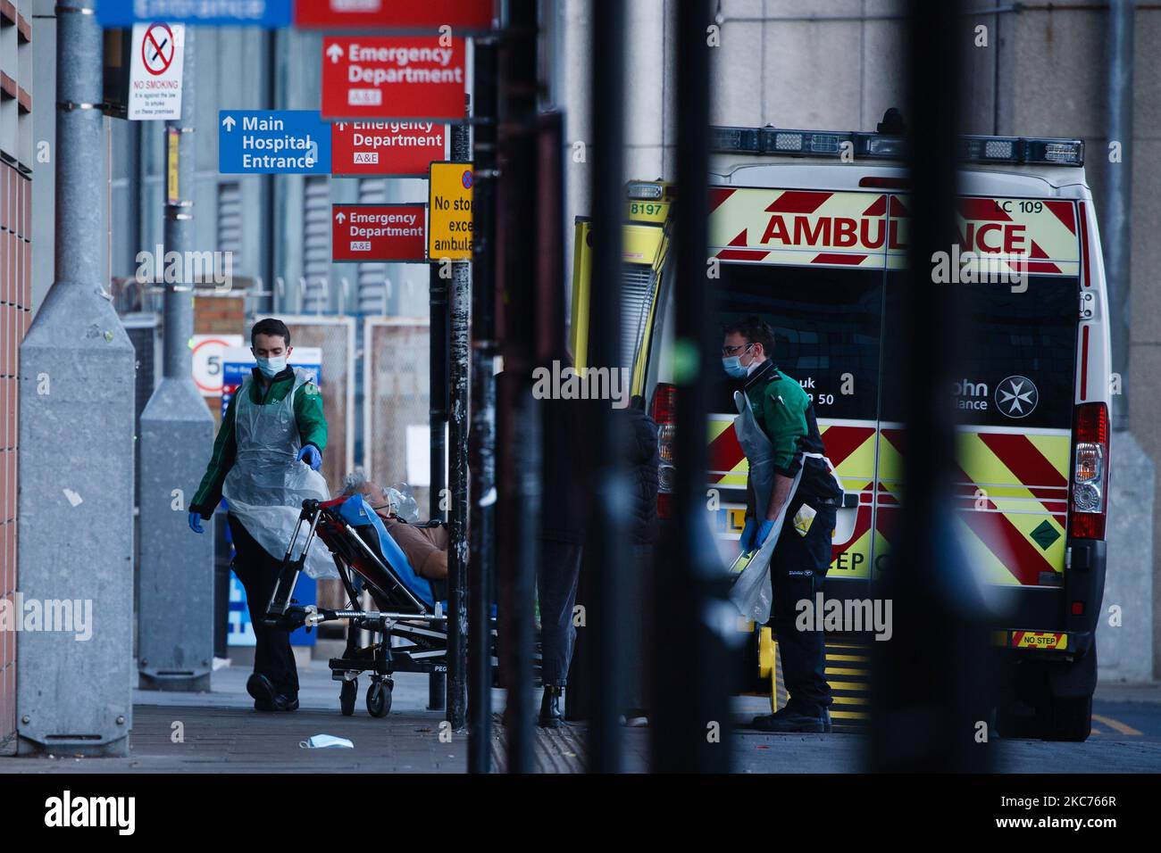 Paramedics wheel a patient wearing an oxygen mask from an ambulance ...