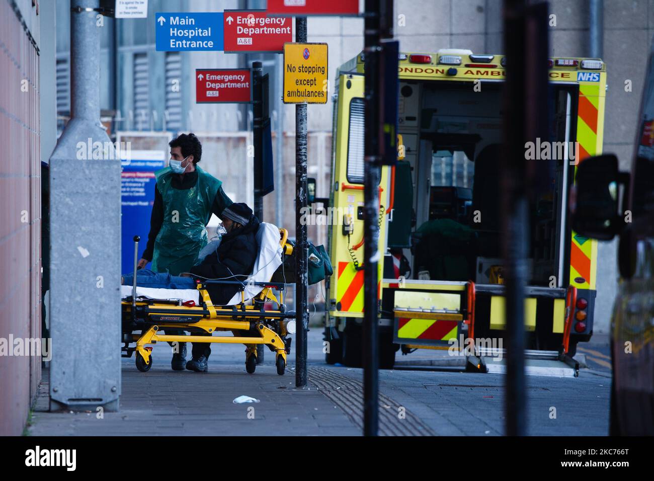 Paramedics wheel a patient wearing an oxygen mask from an ambulance ...