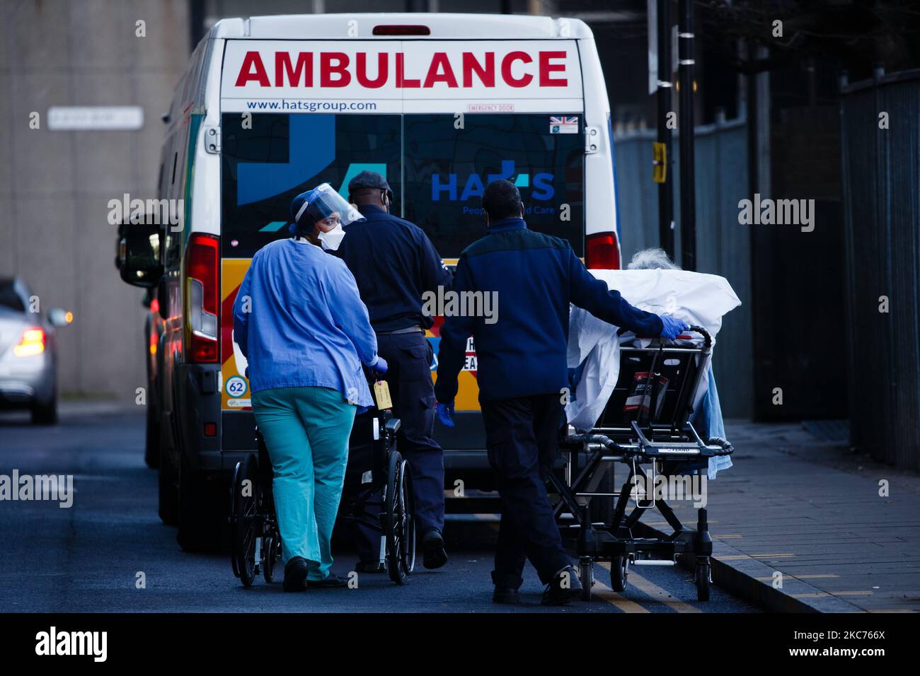 A medic wearing a face mask and visor helps transport a patient into an ...