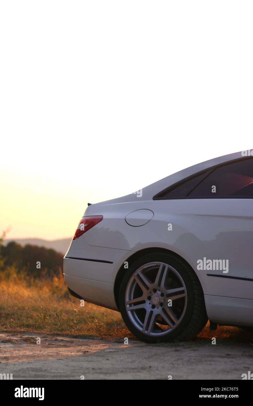 A vertical shot of a white Mercedes Benz E-class car parked on the road ...
